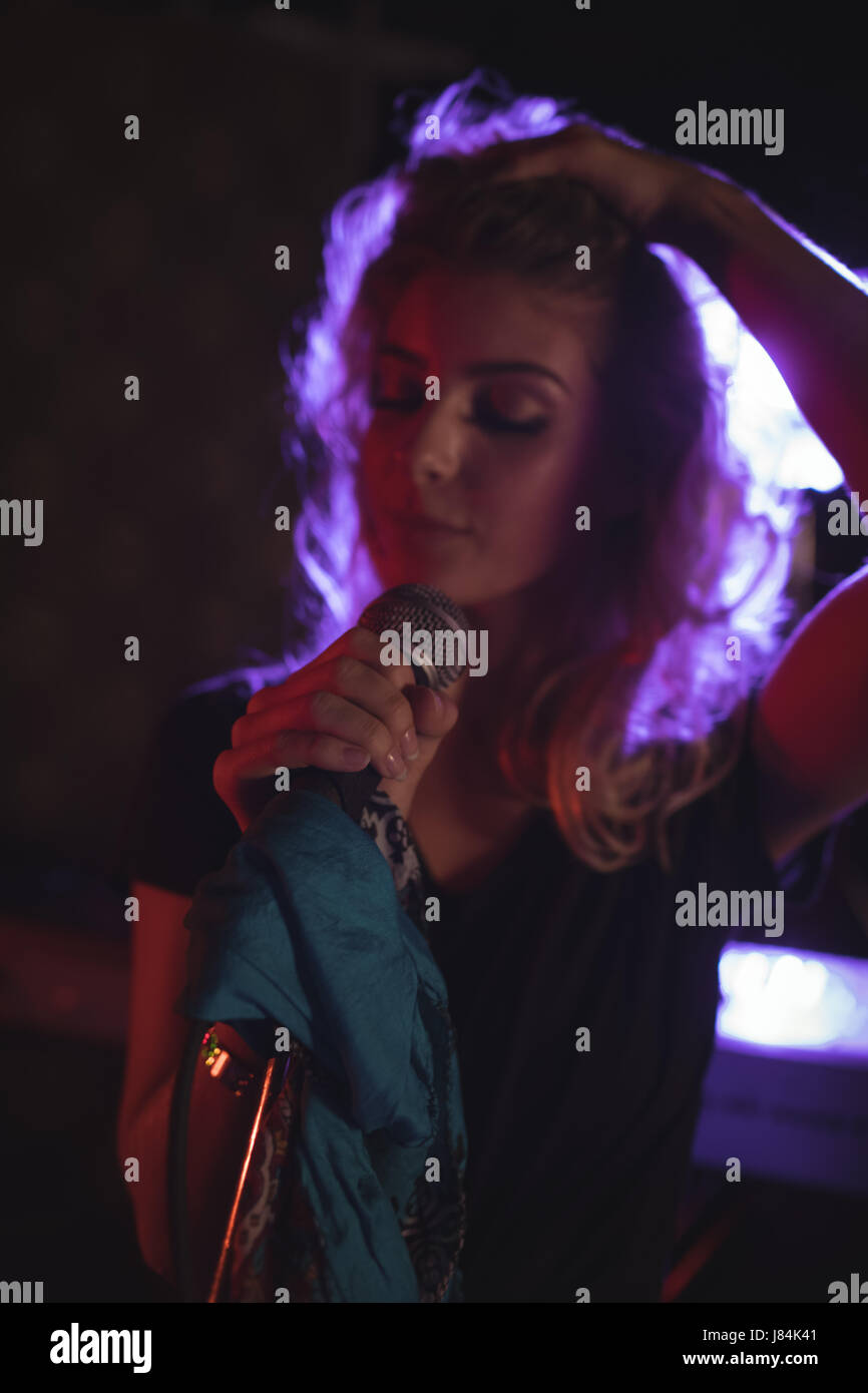 Beautiful female singer with hand in hair performing in illuminated ...