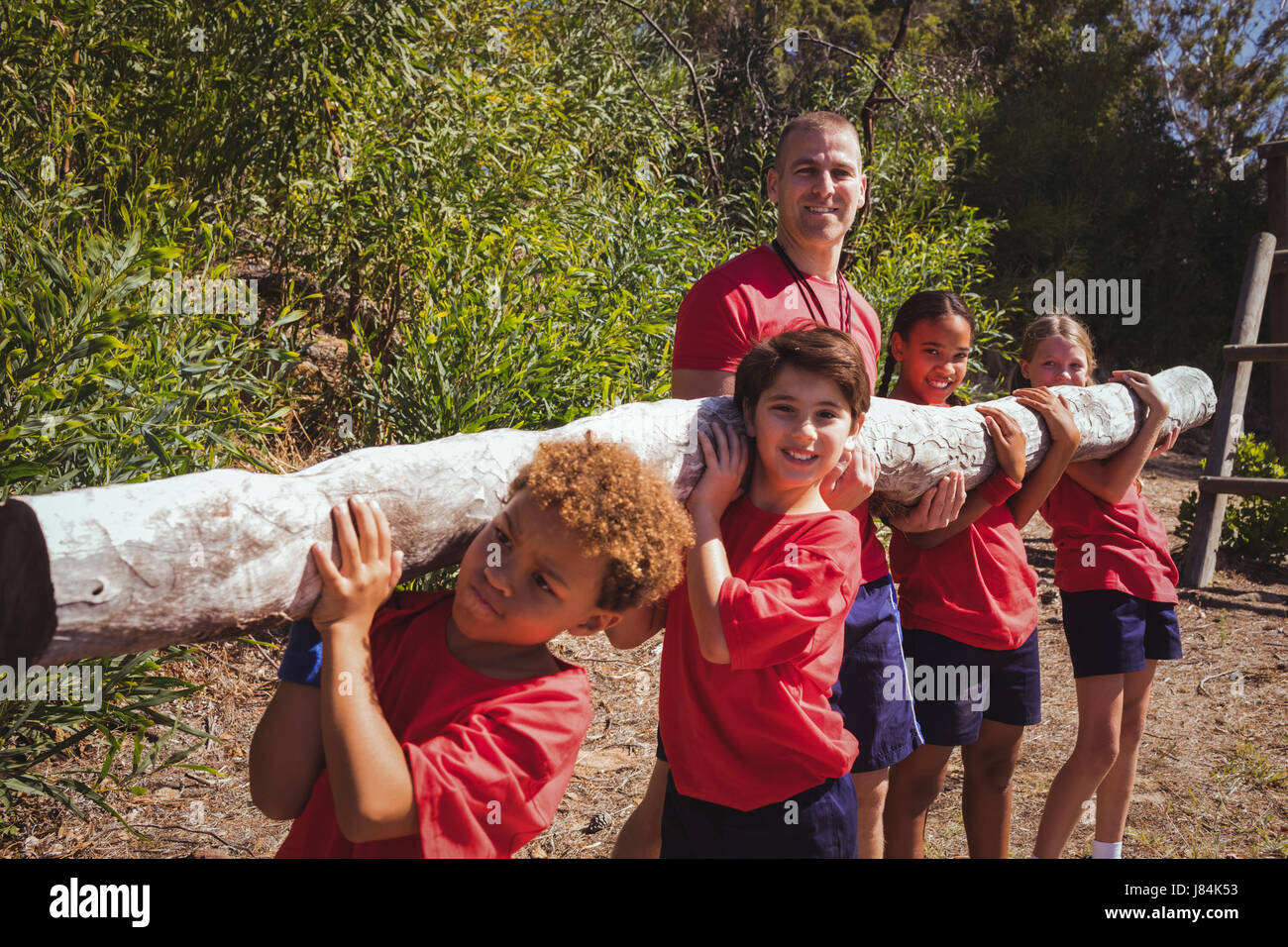 Trainer assisting kids in carrying a heavy wooden log during obstacle ...