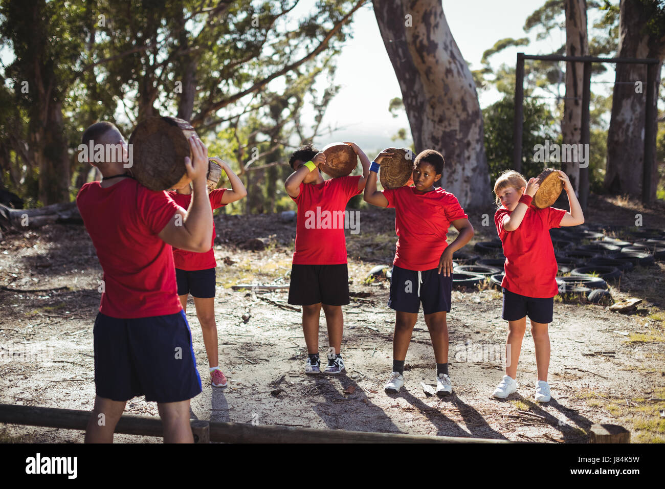 Trainer and kids carrying wooden logs during obstacle course training ...