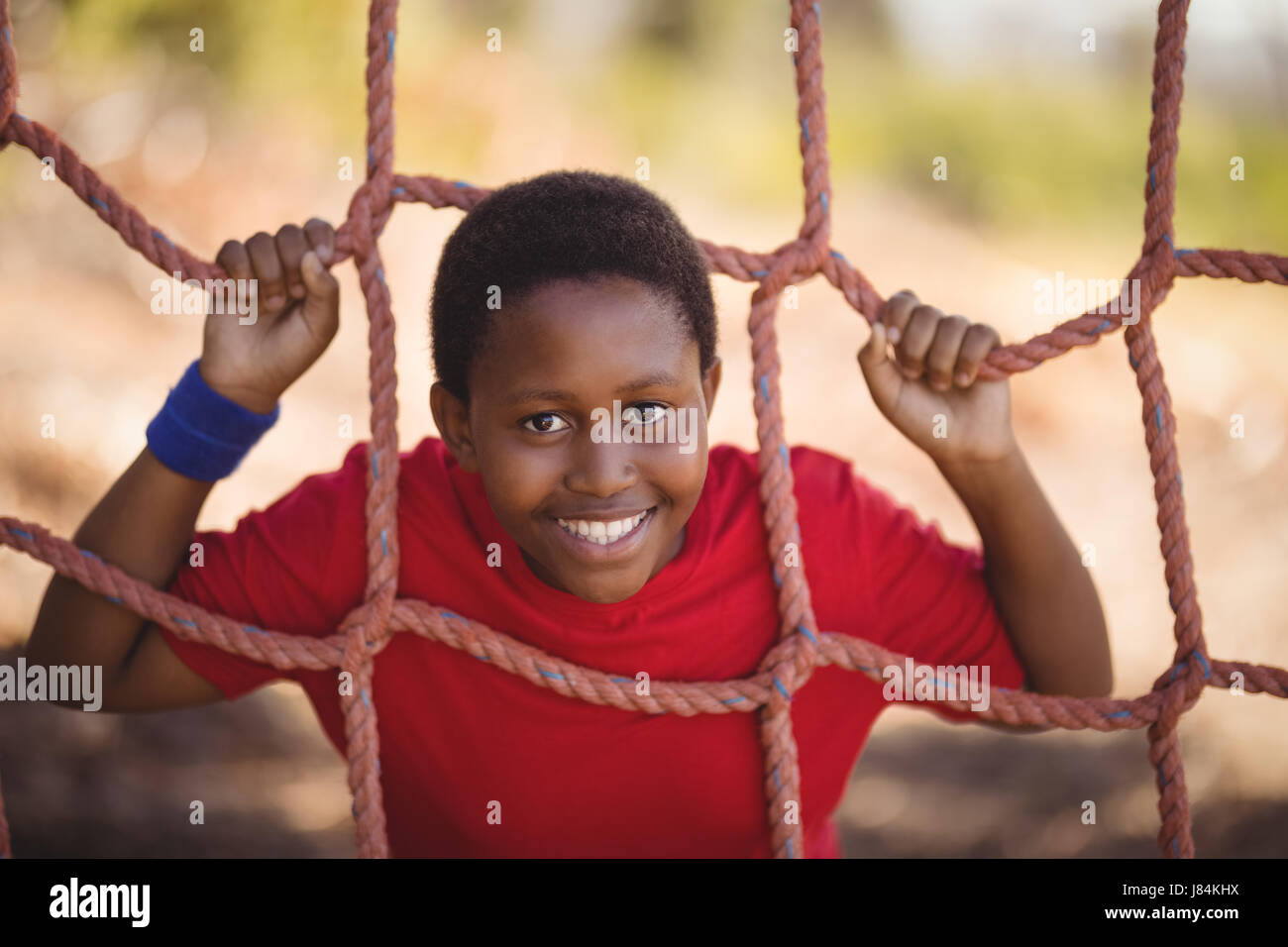 Portrait of happy boy leaning on net during obstacle course in boot ...