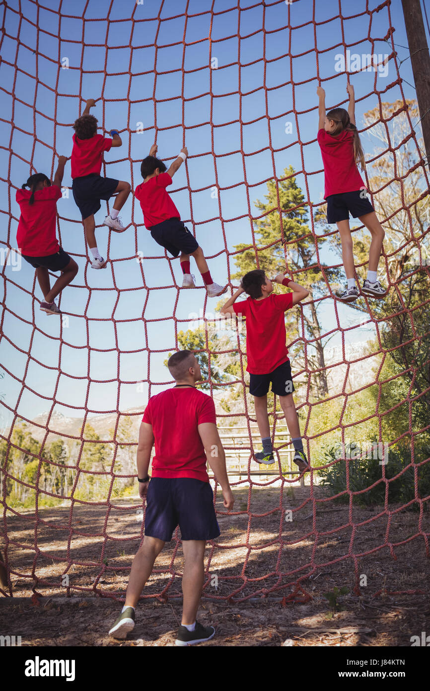 Trainer instructing kids in net climbing during obstacle course ...