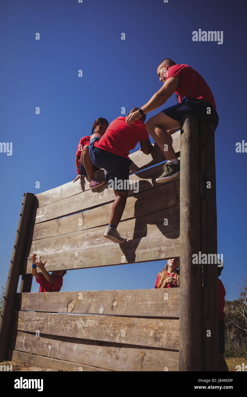 Trainer assisting kids to climb a wooden wall during obstacle course ...