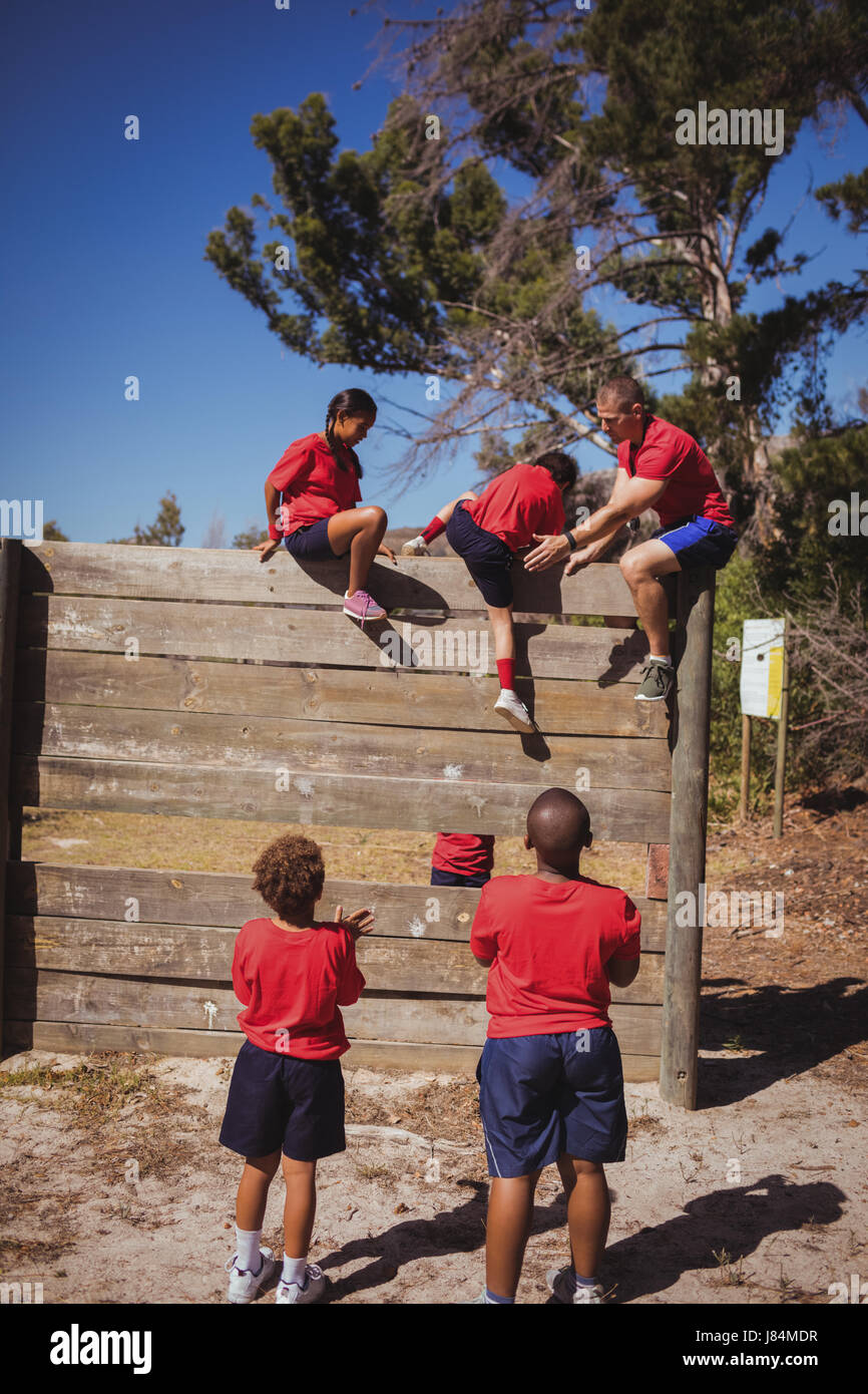 Trainer assisting kids to climb a wooden wall during obstacle course ...