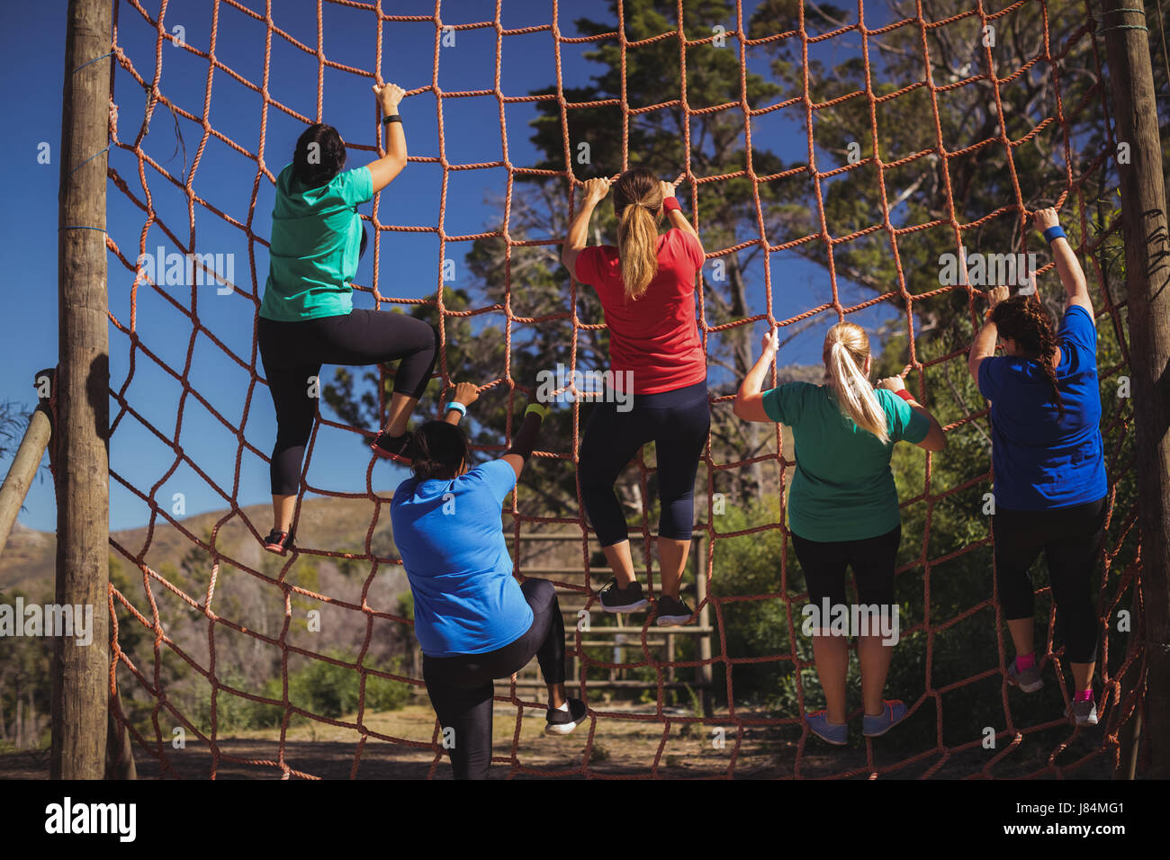 Group of fit woman climbing a net during obstacle course training in ...