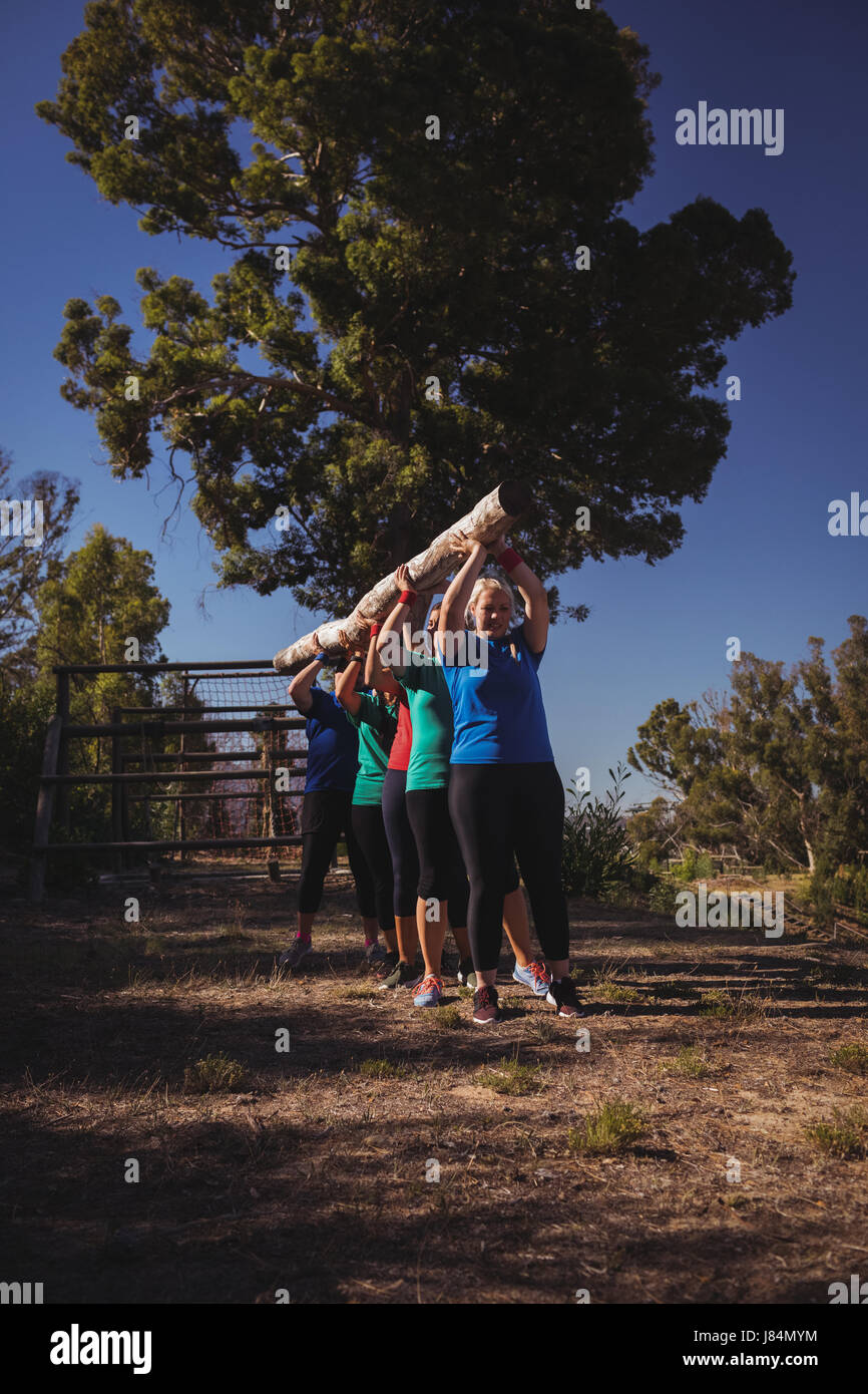 Group of fit women carrying a heavy wooden log during obstacle course ...