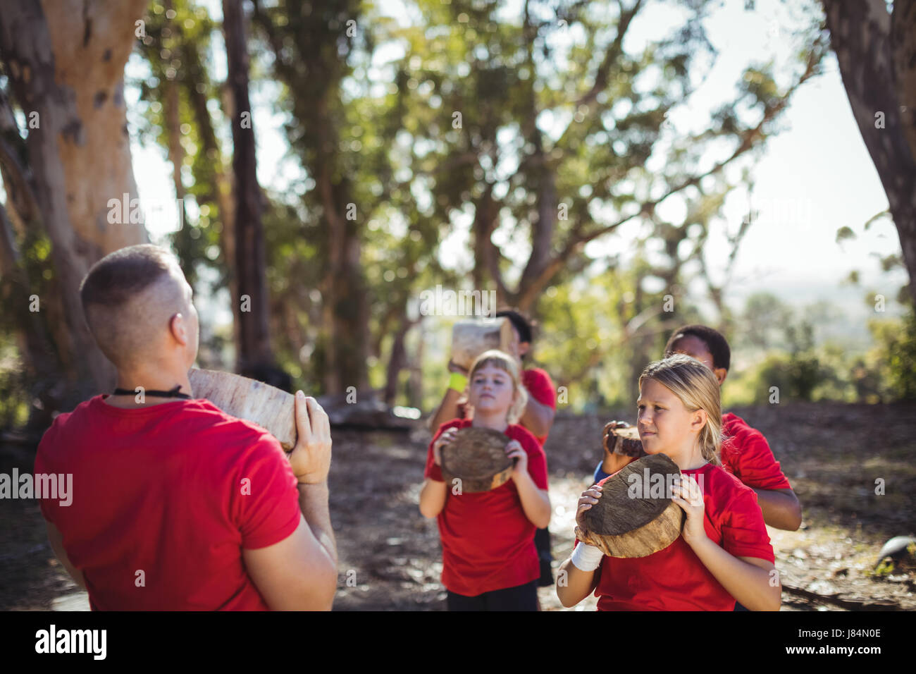 Trainer and kids carrying wooden logs during obstacle course training ...