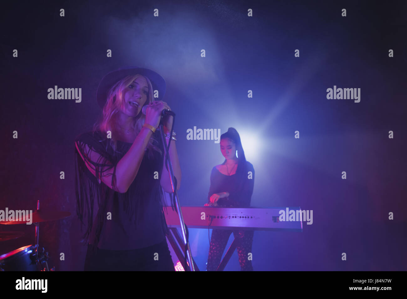 Female singer singing while musician playing piano in illuminated ...