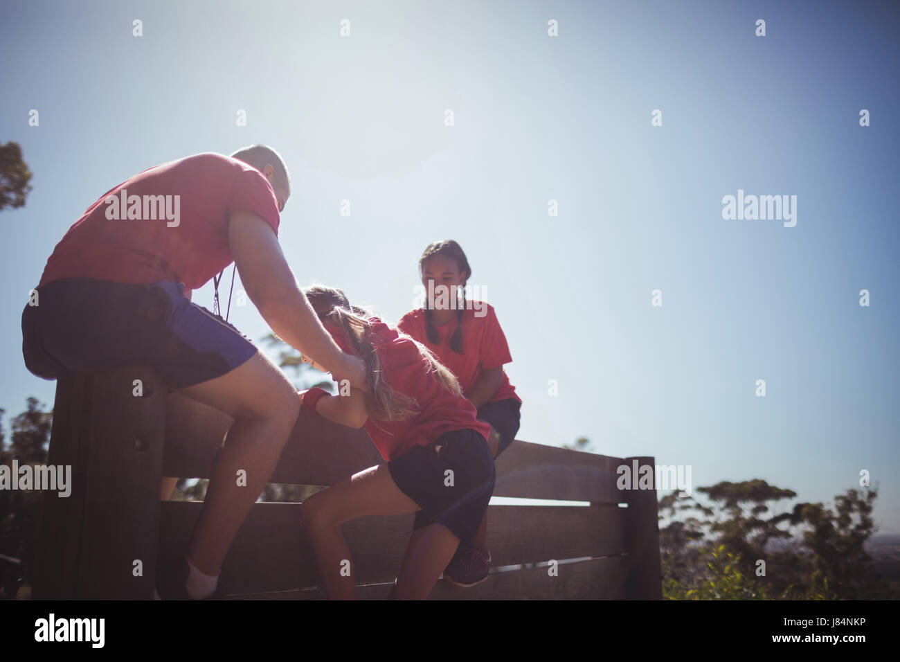 Trainer assisting kids to climb a wooden wall during obstacle course ...