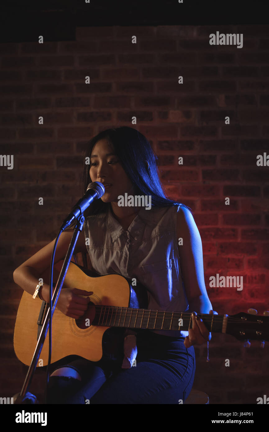 Smiling female singer playing guitar while performing in nightclub ...