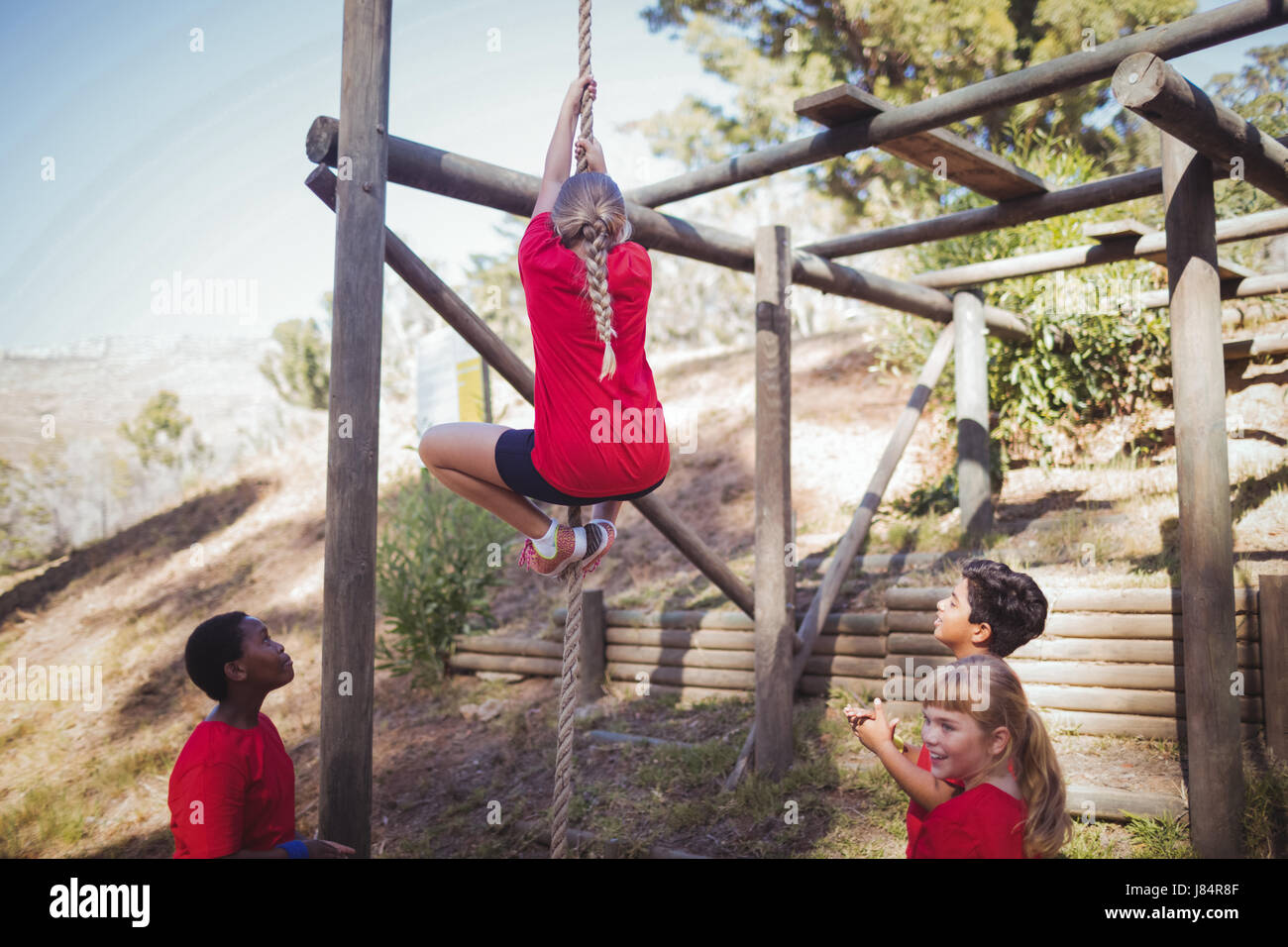 Girl climbing a rope during obstacle course training in the boot camp ...