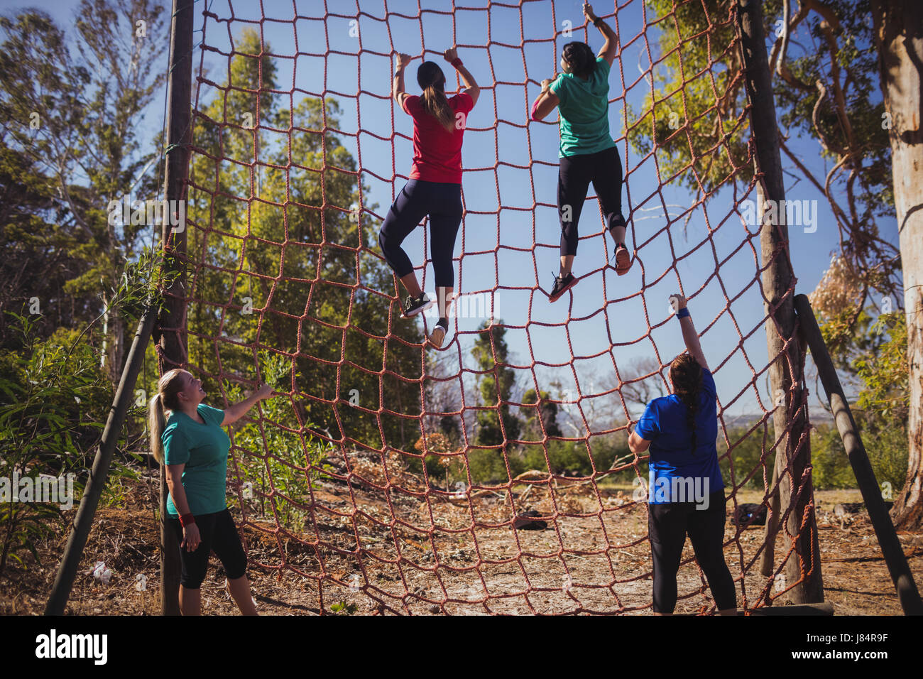 Group of fit woman climbing a net during obstacle course training in ...