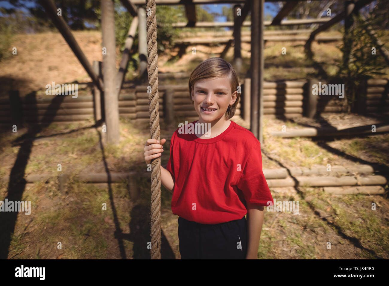 Portrait of smiling girl holding rope during obstacle course in boot ...