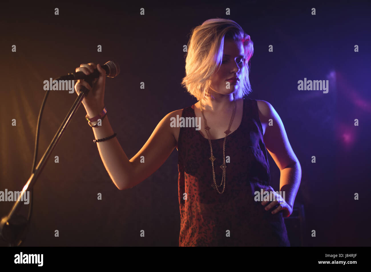 Confident female singer holding microphone in illuminated nightclub ...