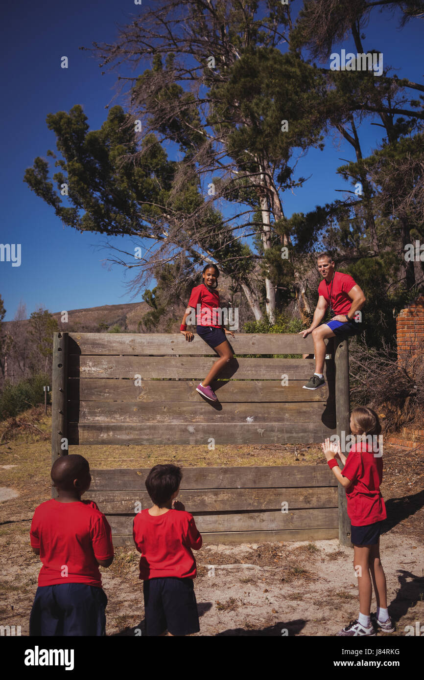 Trainer assisting kids to climb a wooden wall during obstacle course ...