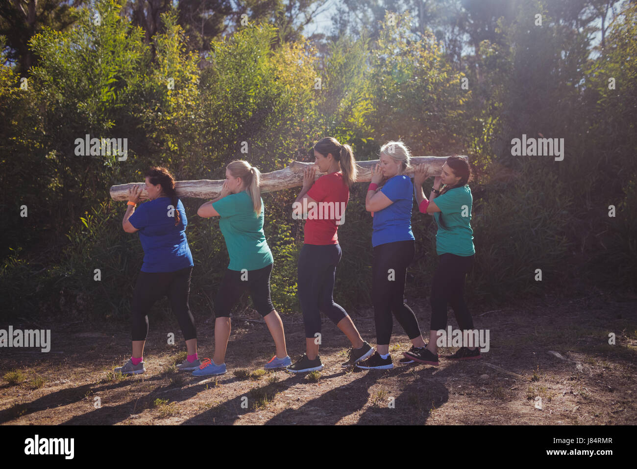 Group of fit women carrying a heavy wooden log during obstacle course ...