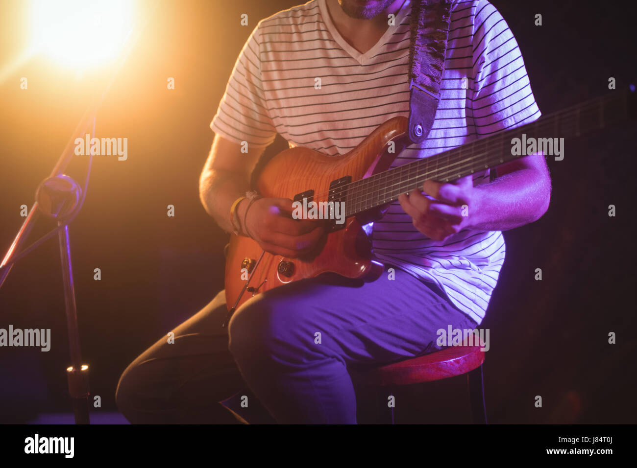 Mid section of male singer playing guitar in illuminated nightclub ...