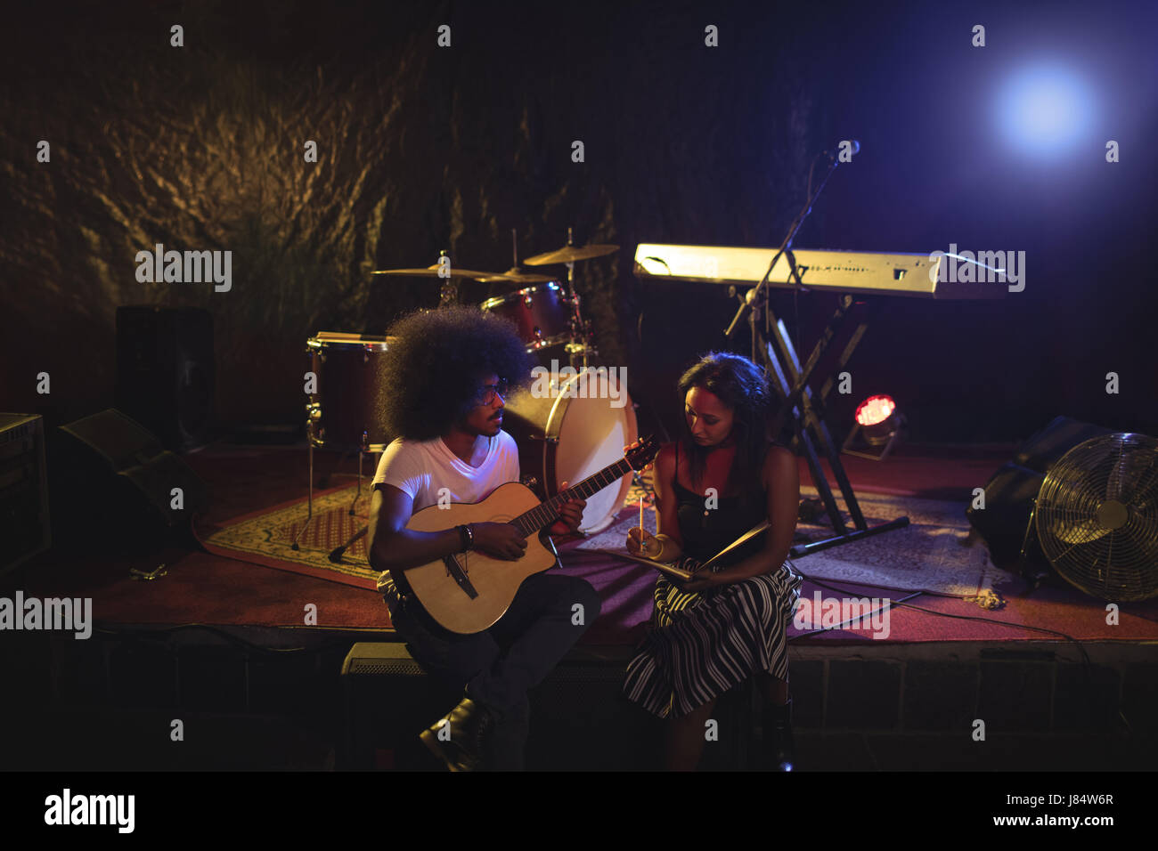Musicians practicing while sitting on illuminated stage in nightclub ...