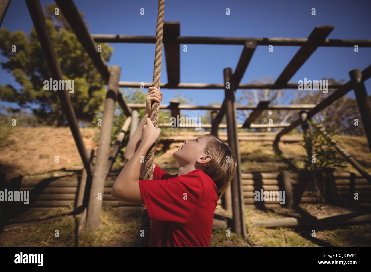 Determined girl climbing rope during obstacle course in boot camp Stock ...