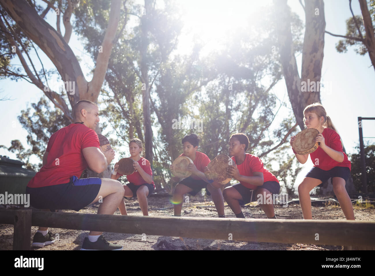 Trainer and kids carrying wooden logs during obstacle course training ...