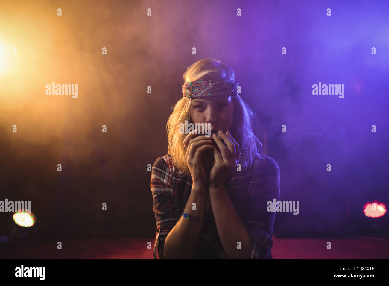 Portrait of confident female musician playing harmonica in illuminated ...