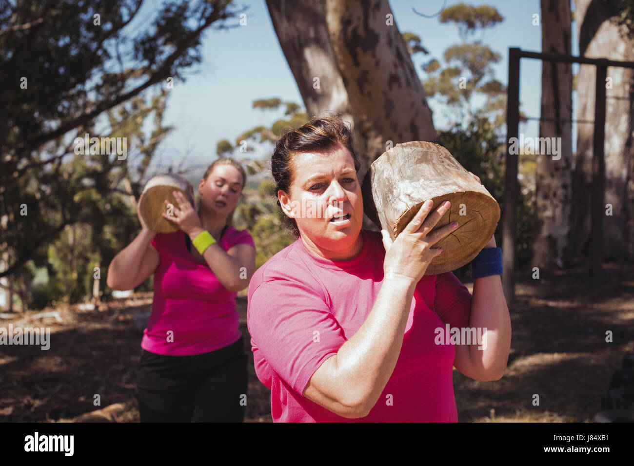 Two women carrying a heavy wooden log during obstacle course in the ...