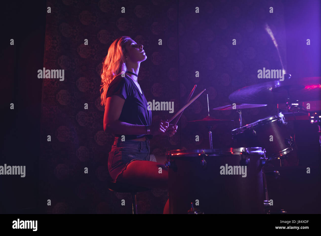 Side view of young female drummer performing in illuminated nightclub ...