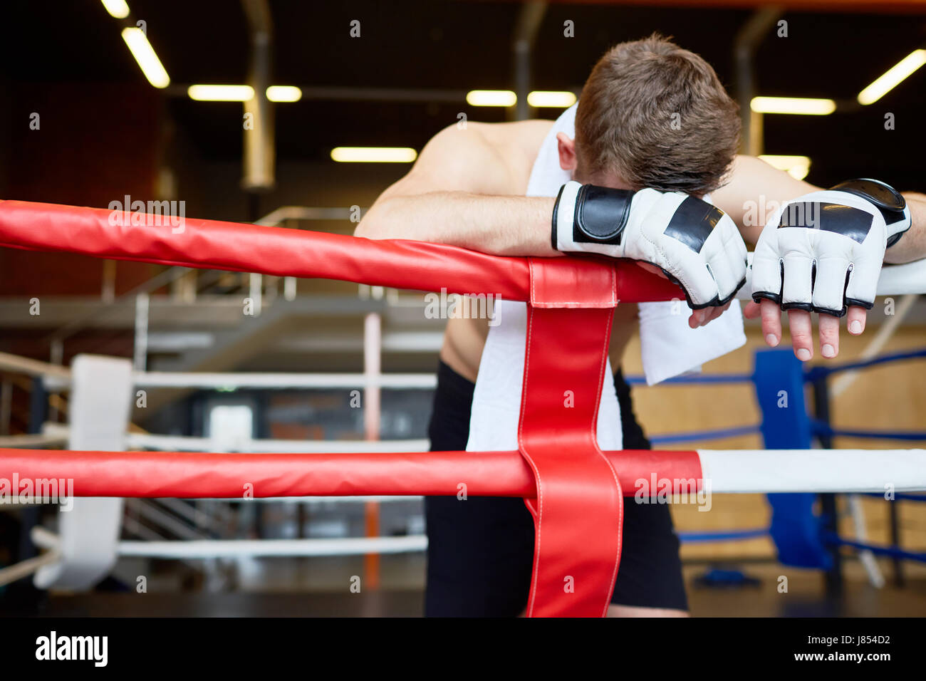 Defeated kick-boxer leaning on boxing-ring rope Stock Photo - Alamy