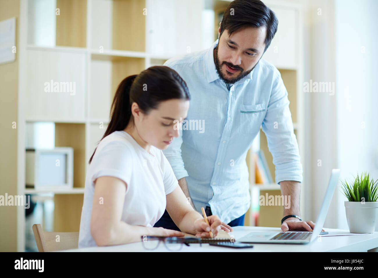 Portrait of Asian man helping young woman working with laptop in office ...