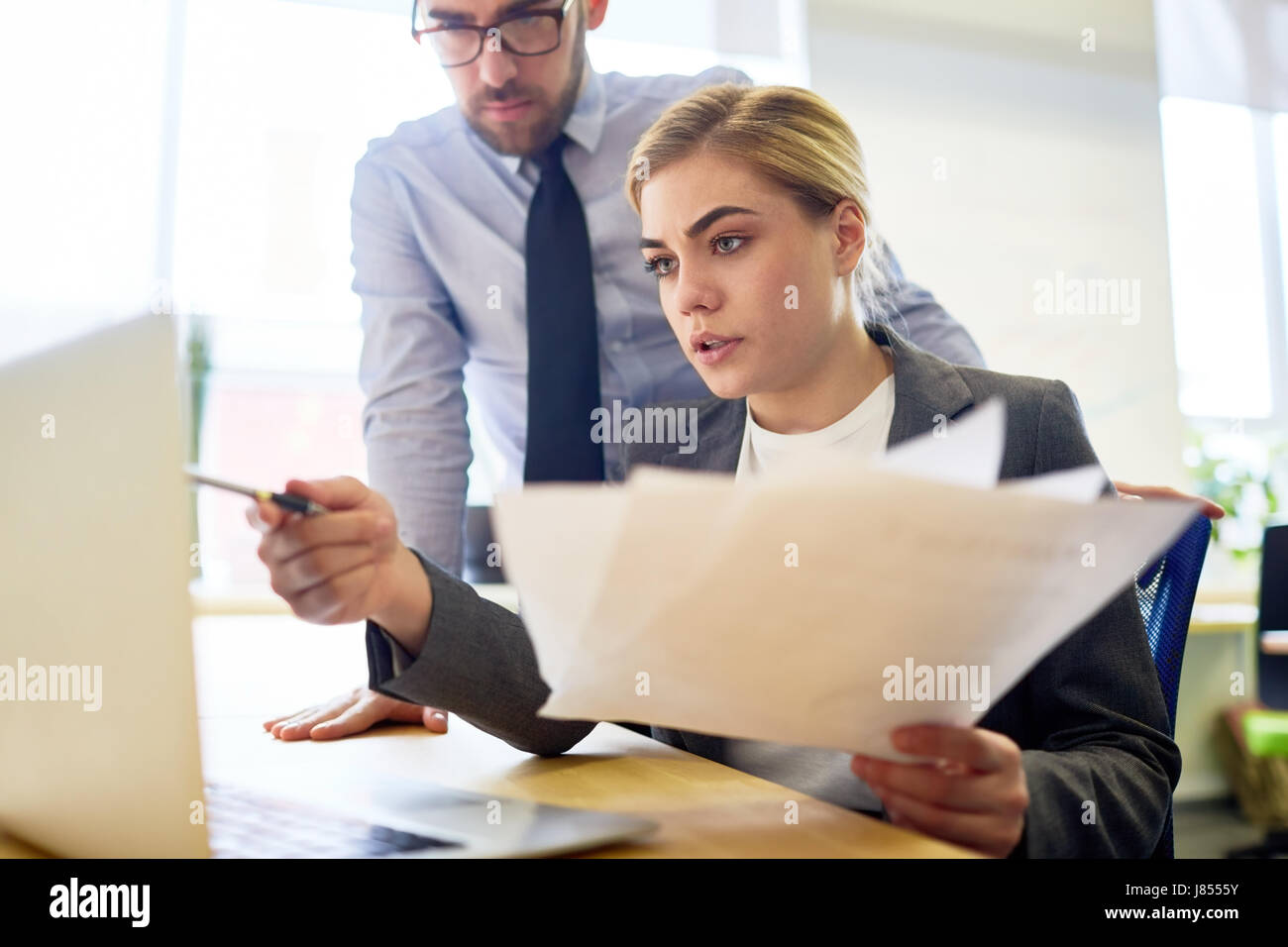 Confident employee with papers pointing at laptop screen during ...