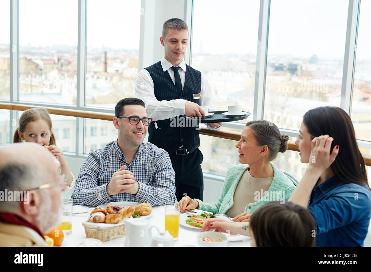 Young waiter serving family in restaurant Stock Photo - Alamy