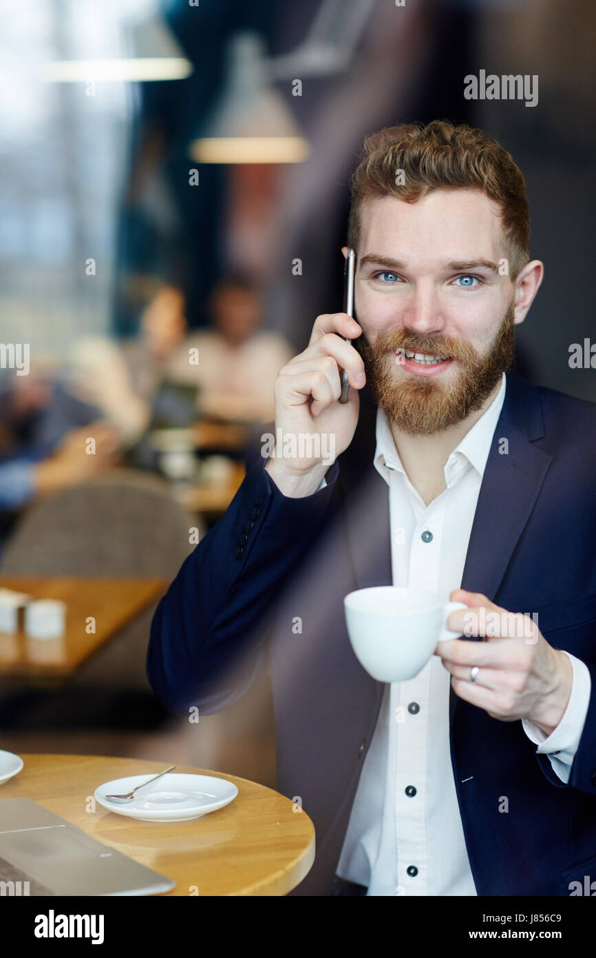 Portrait of handsome young businessman speaking by phone in cafe and ...