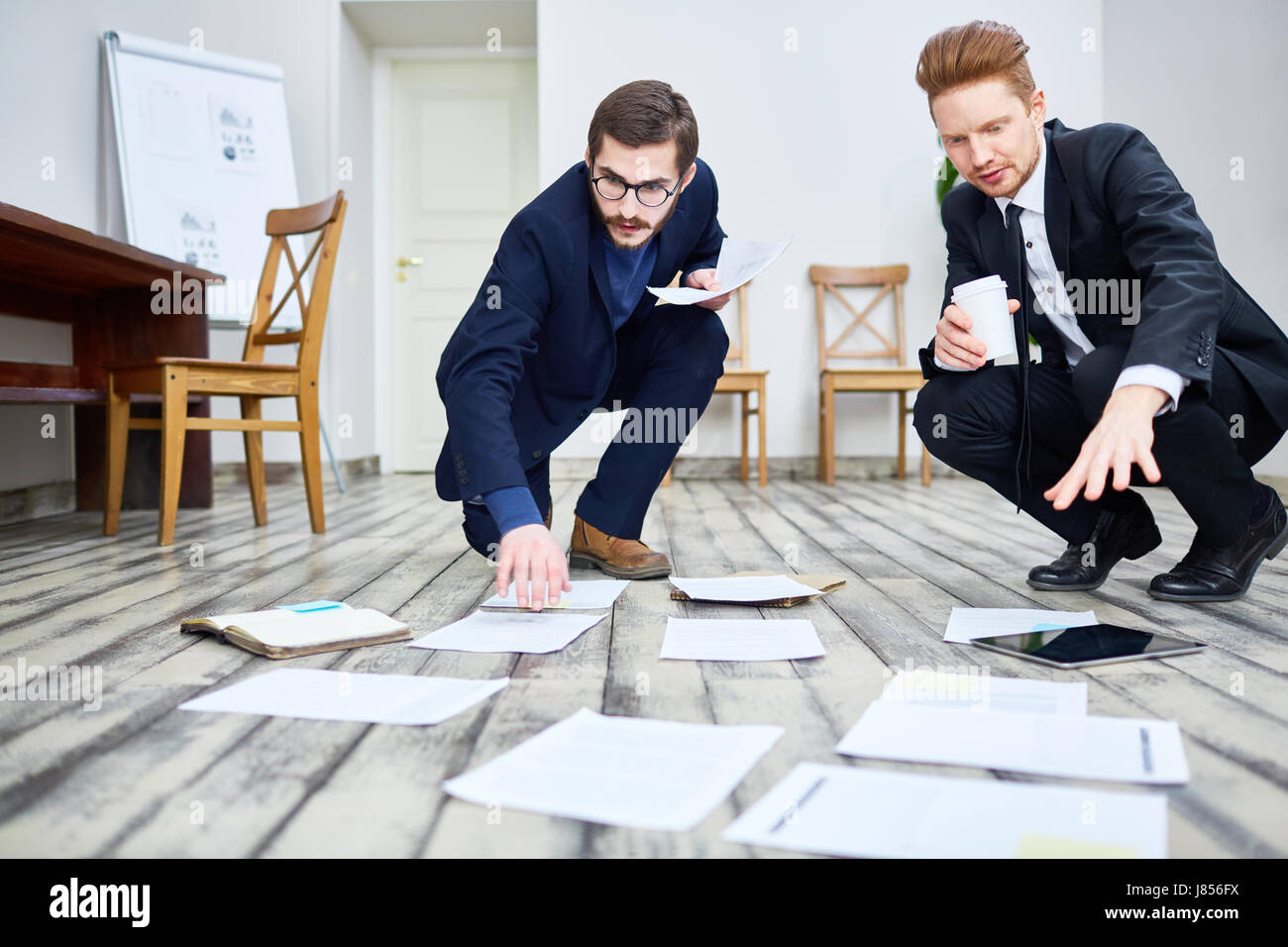 Portrait of two business men sorting documents on floor in office while ...