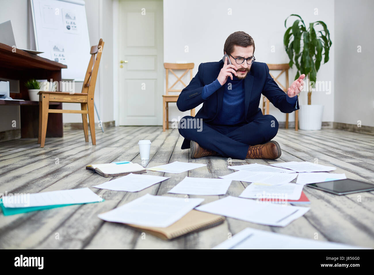Portrait of bearded man speaking by phone angrily and sorting documents ...