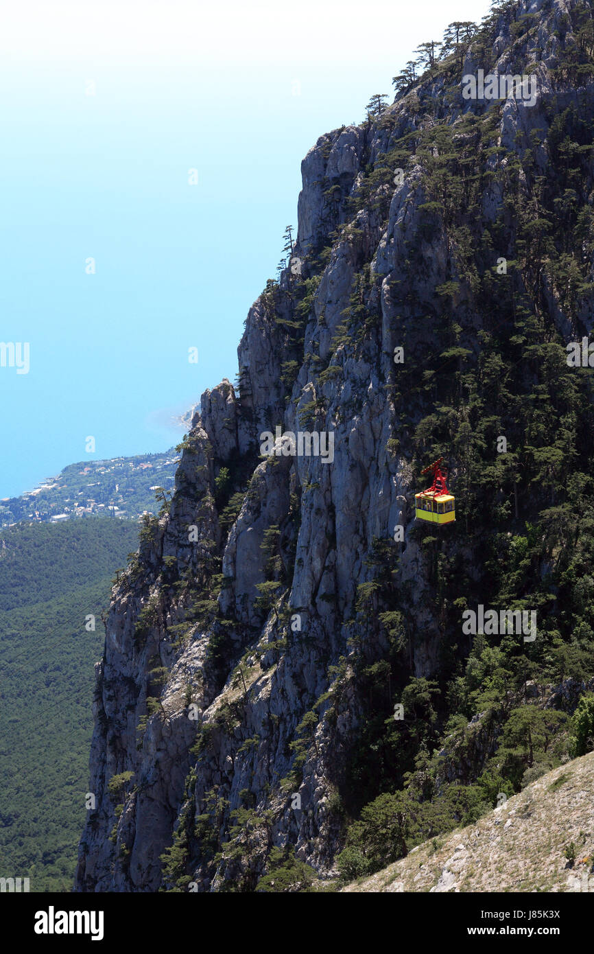 Yellow overhead cable car on background with very high mountain and sea ...