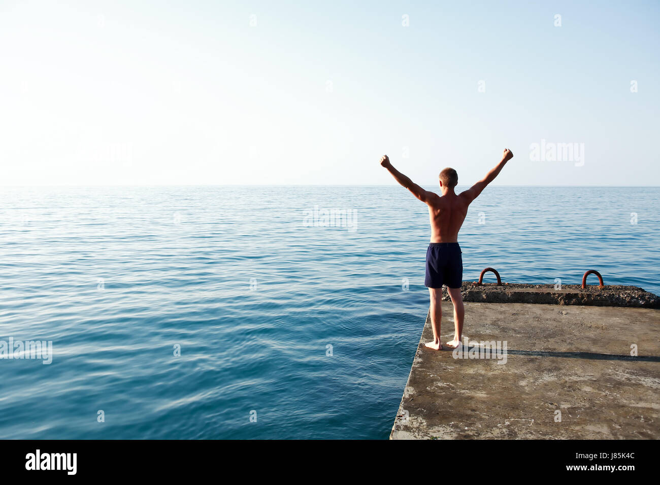 Teenage boy standing on pier against sea with hands up Stock Photo - Alamy