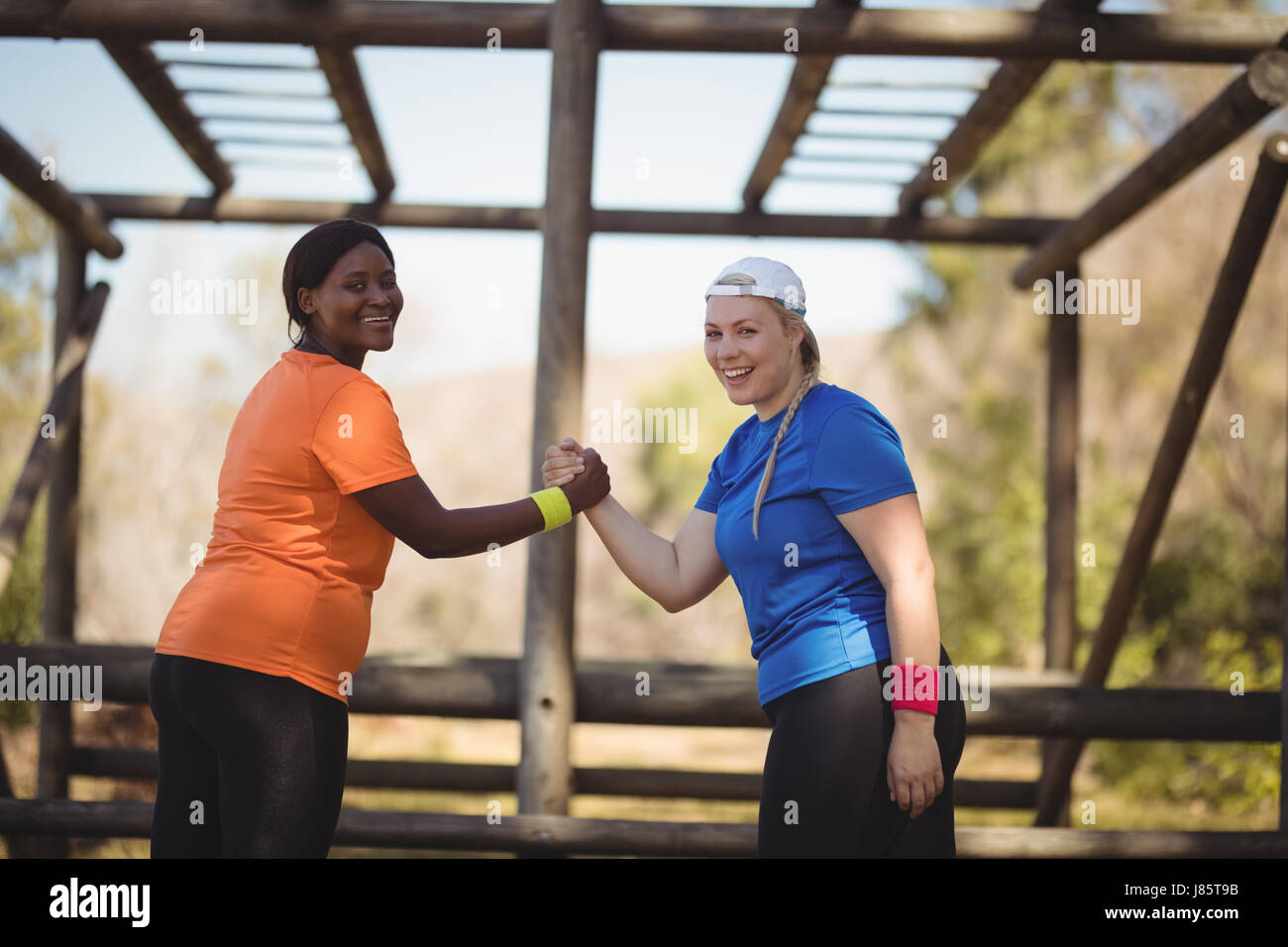 Portrait of happy friend holding hands during obstacle course in boot ...