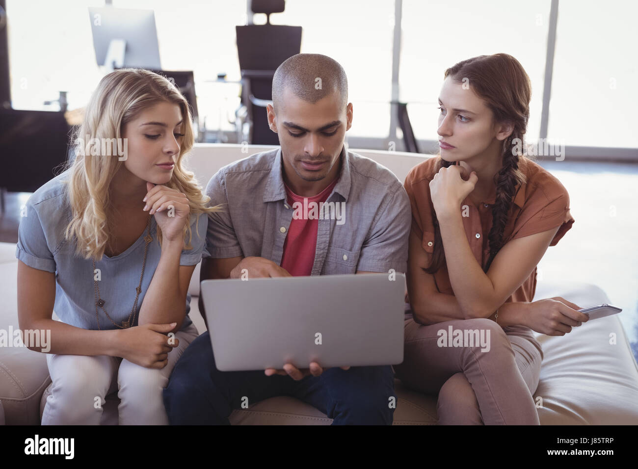 Serious young business colleagues working together over laptop while ...