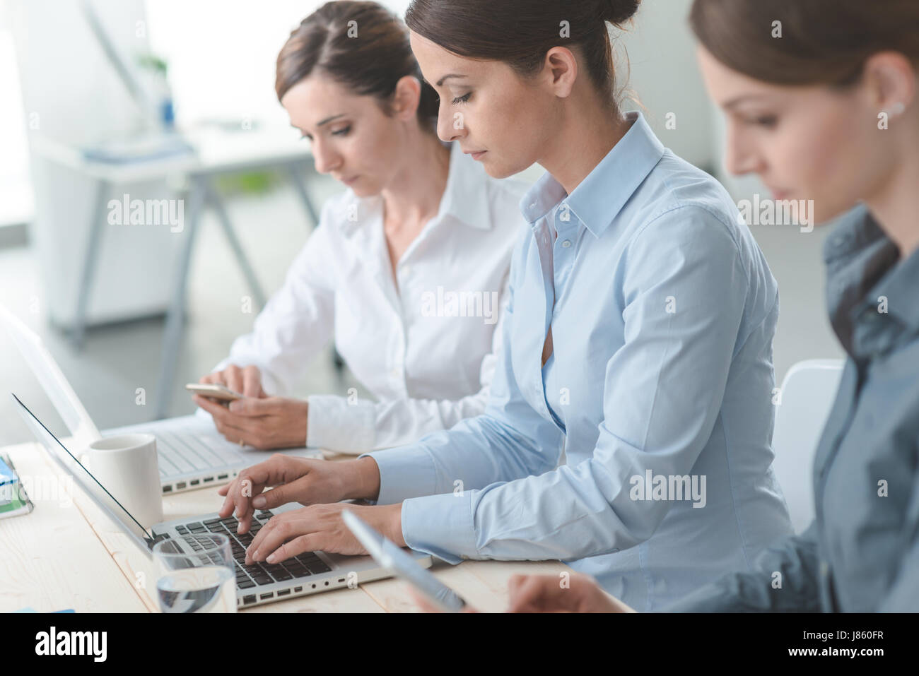 Efficient business women working together at office desk using laptops ...