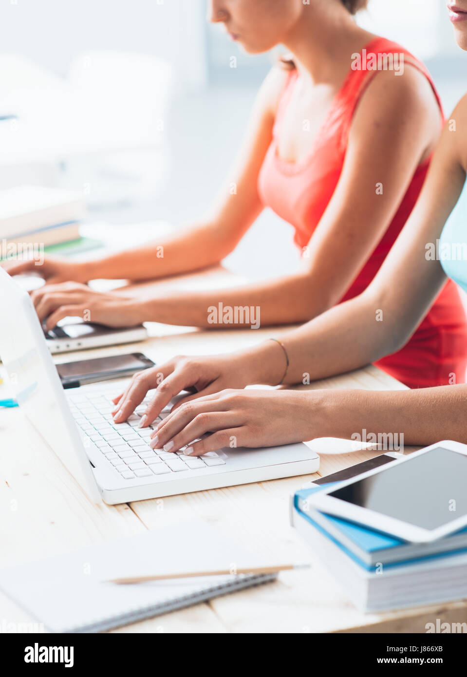 Young students doing homework sitting at desk and typing on laptops ...