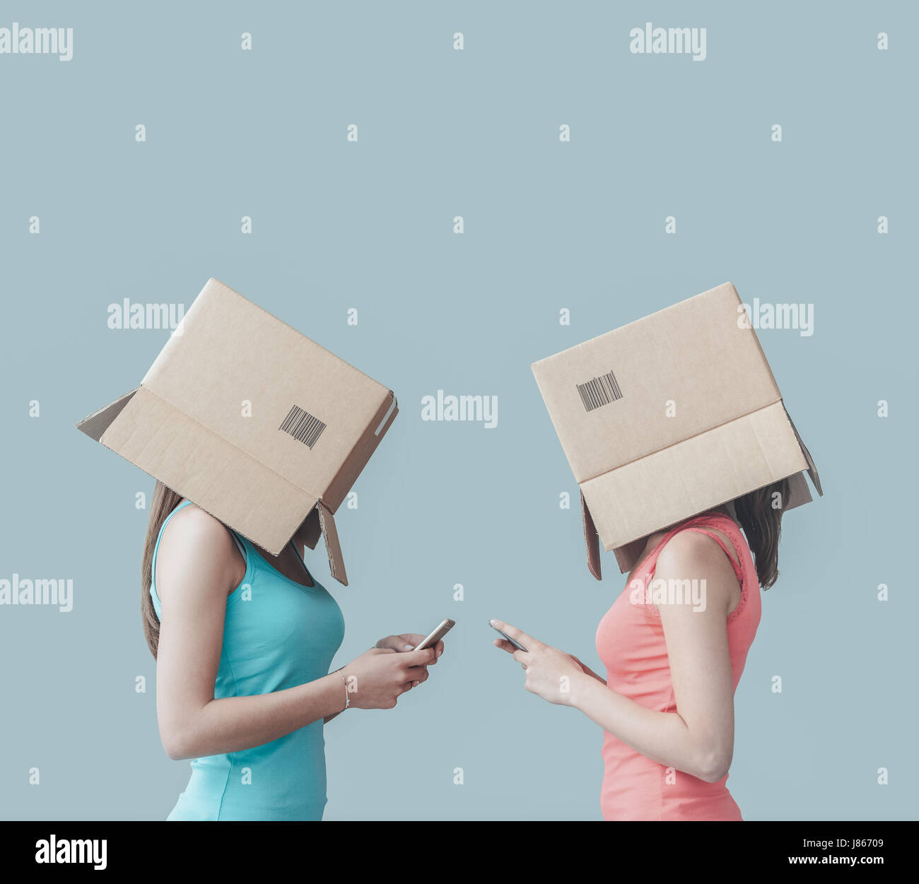 Adolescent girls with boxes on their heads texting with their smart ...