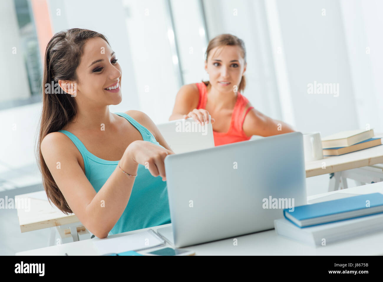 Young female students using laptops at school, one is pointing at the ...