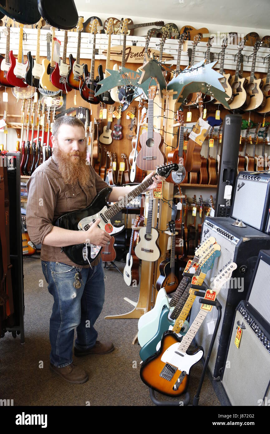 Interior of music store with wall display of guitars. Store owner with ...