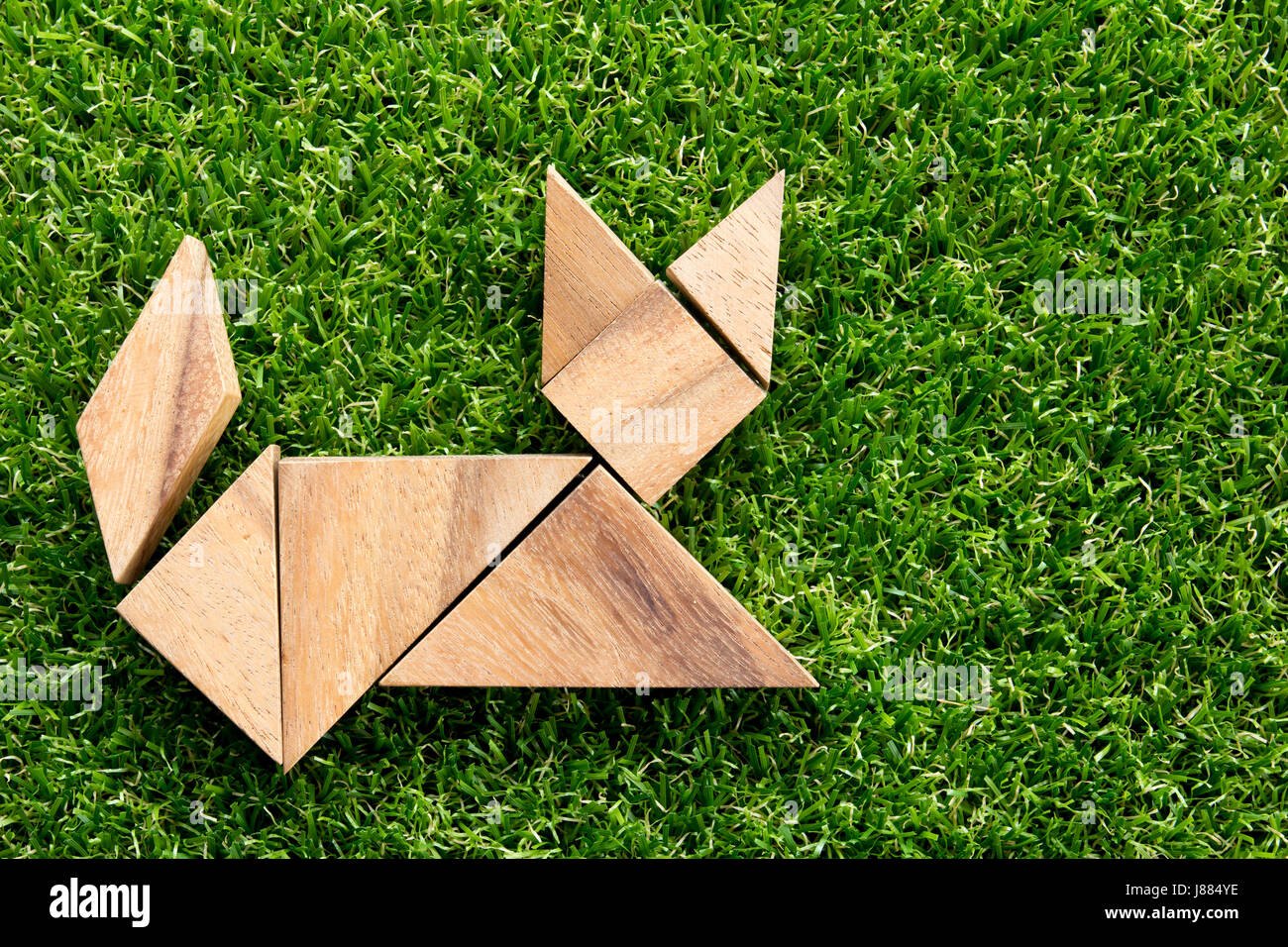 Wooden tangram puzzle in cat shape on artificial green grass background ...