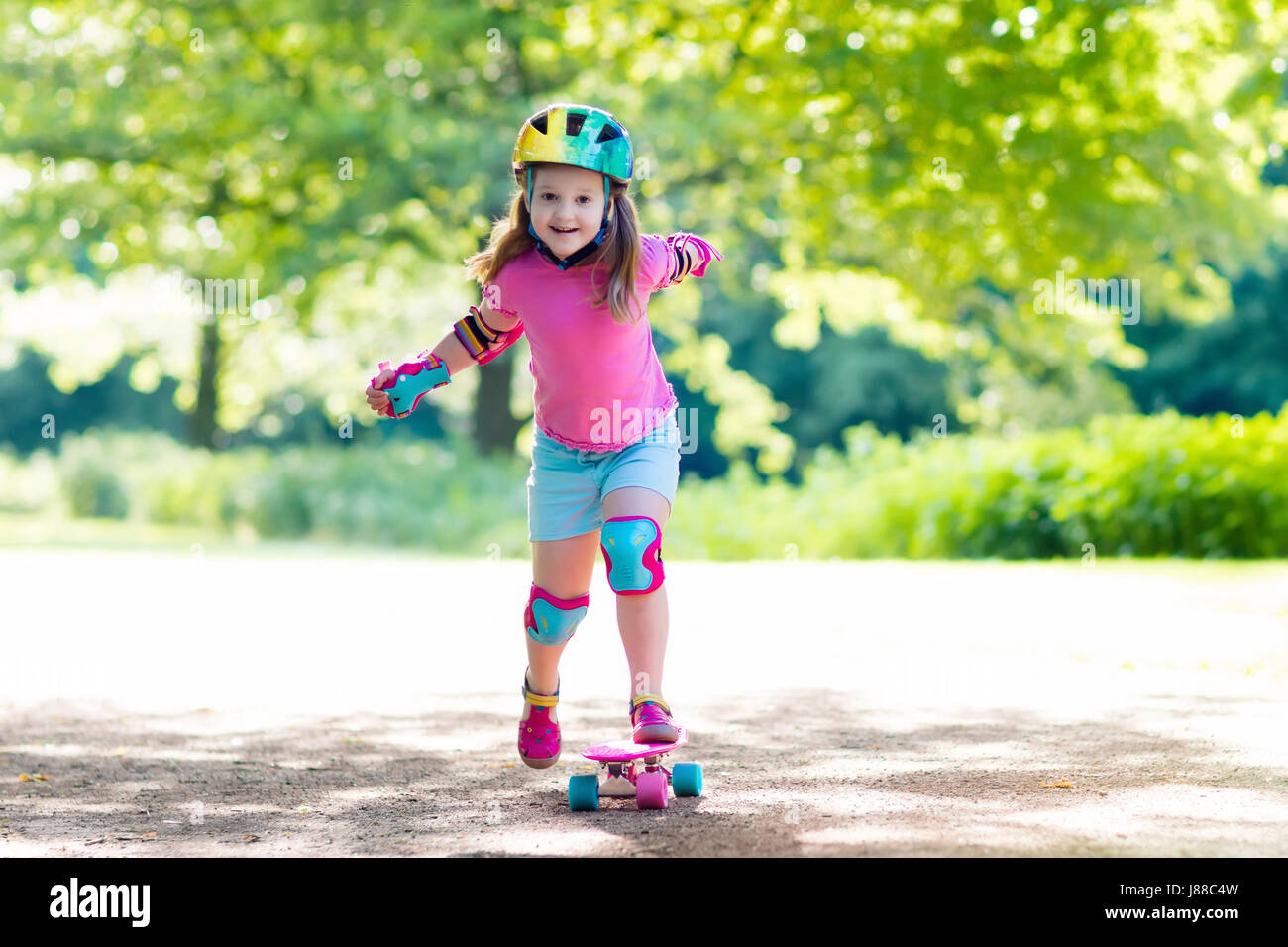 Child riding skateboard in summer park. Little girl learning to ride ...