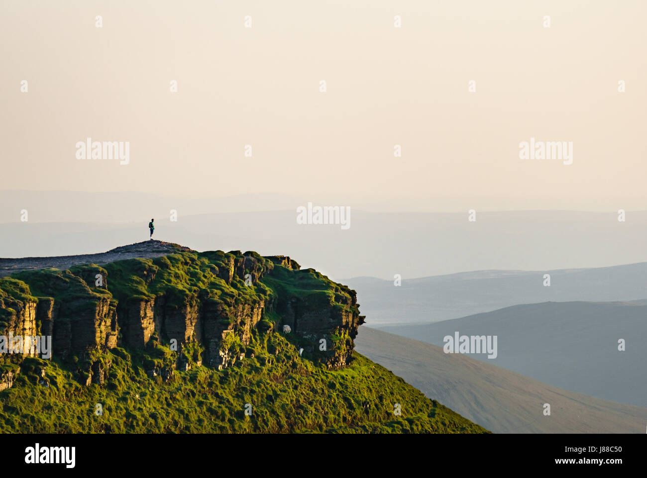 Man standing on a cliff looking out over the valley during sunset. Shot ...