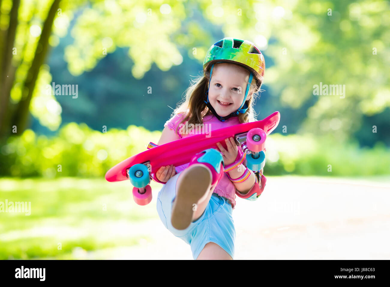 Child riding skateboard in summer park. Little girl learning to ride ...