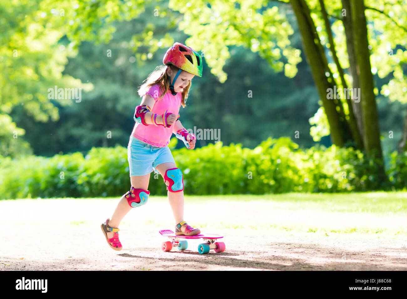 Child riding skateboard in summer park. Little girl learning to ride ...