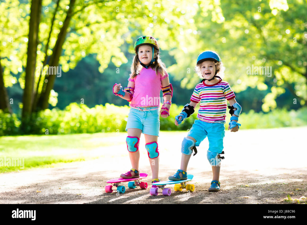 Children riding skateboard in summer park. Little girl and boy learn to ...