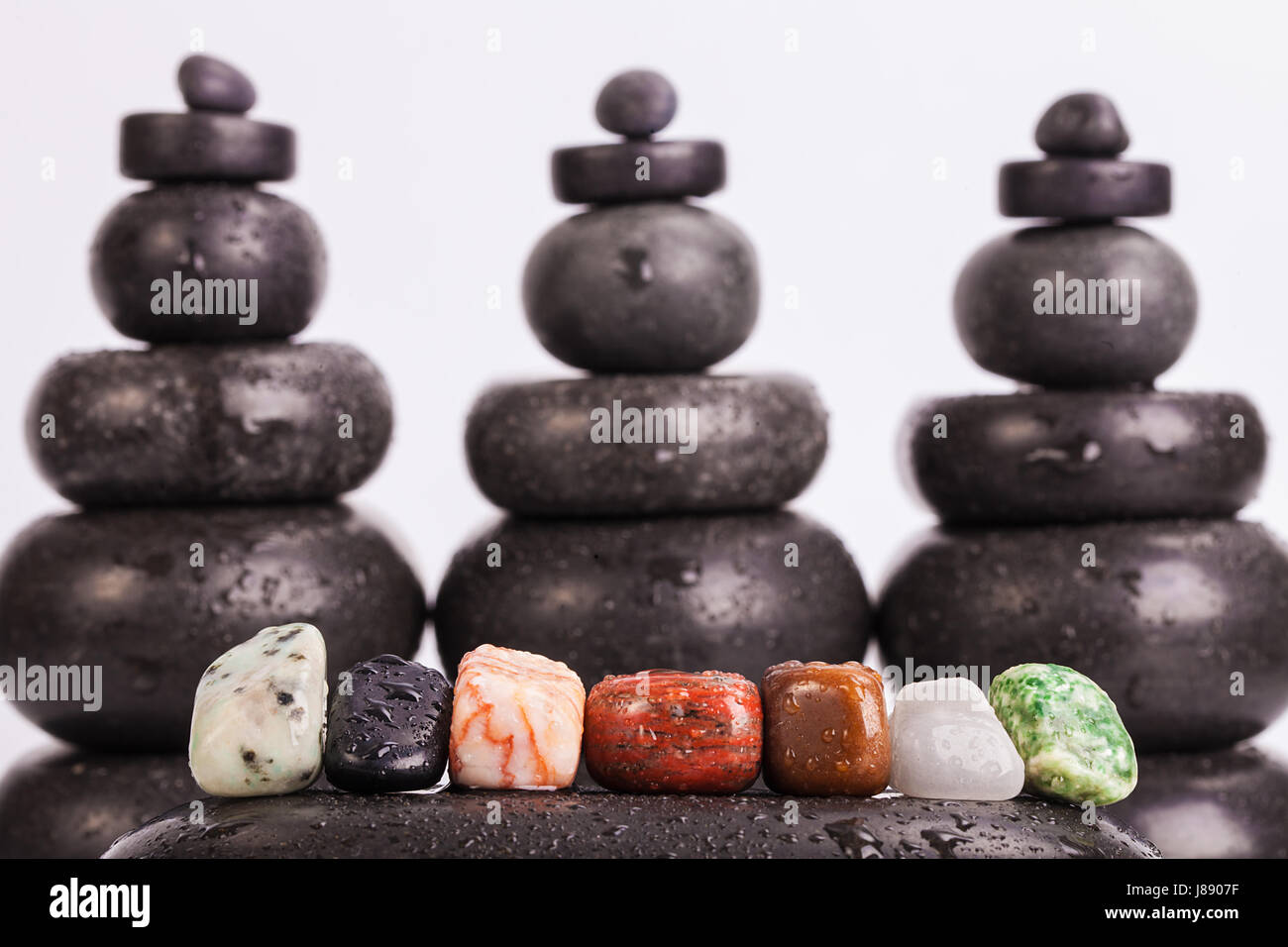 Row of seven chakra colored crystals lined in a row on wet smooth ...