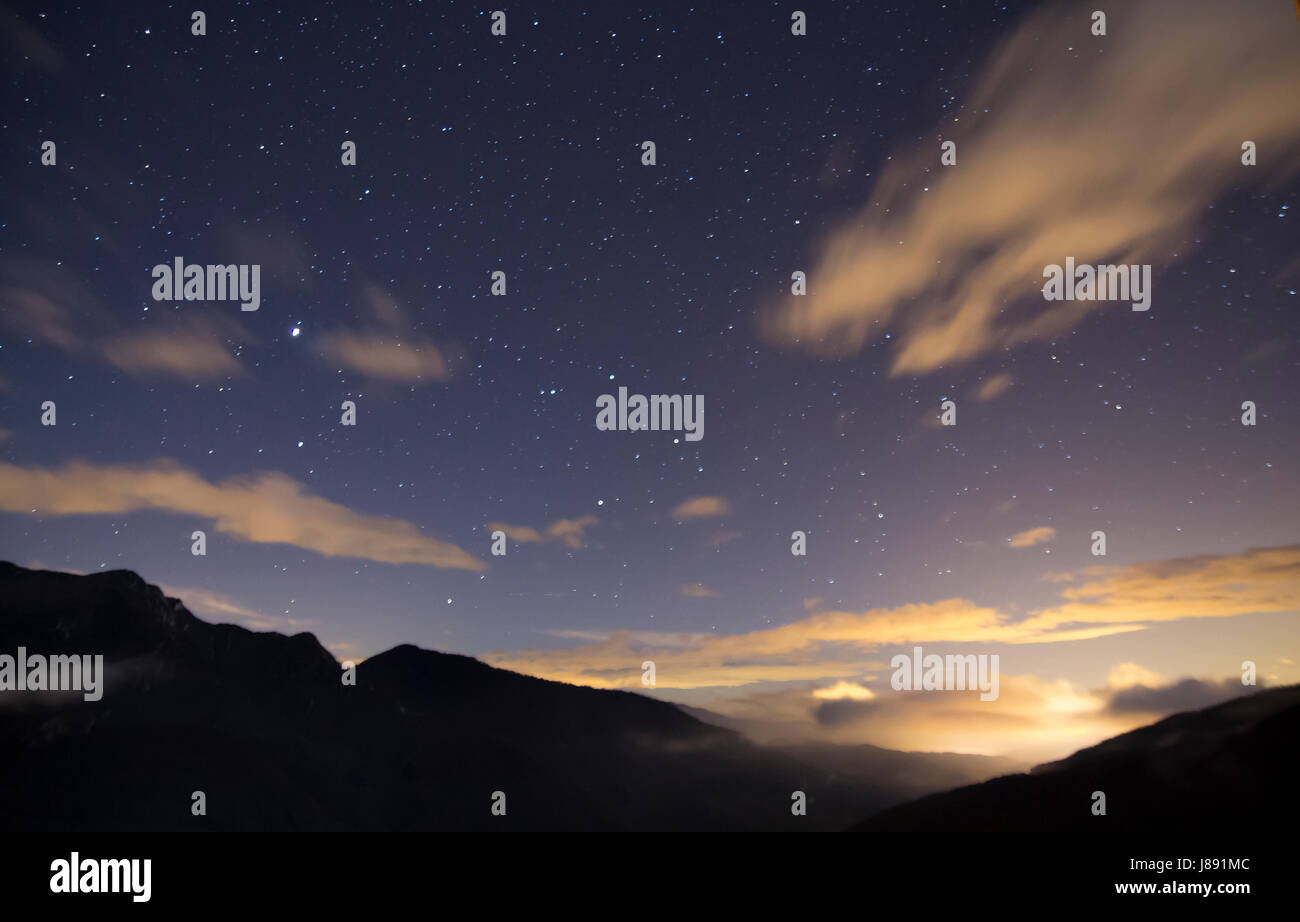 Night landscape with stars and illuminated village in the mountains ...